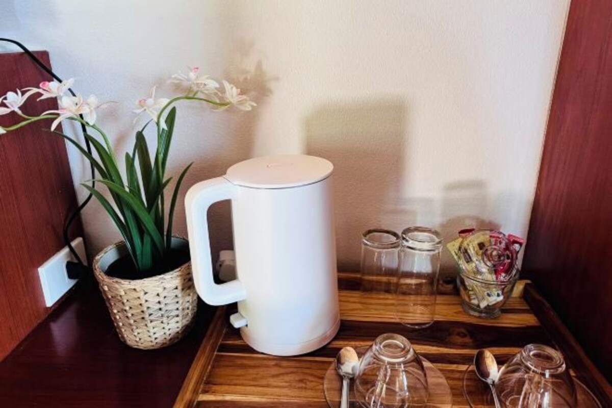 Uma área de cozinha com uma cafeteira branca, uma cesta de vime com uma planta e vários recipientes de vidro sobre uma bandeja de madeira.