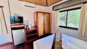 Quarto de hotel com cama, TV exibindo 'NETFLIX', guarda-roupa, secretária pequena com chaleira e janela com cortinas.