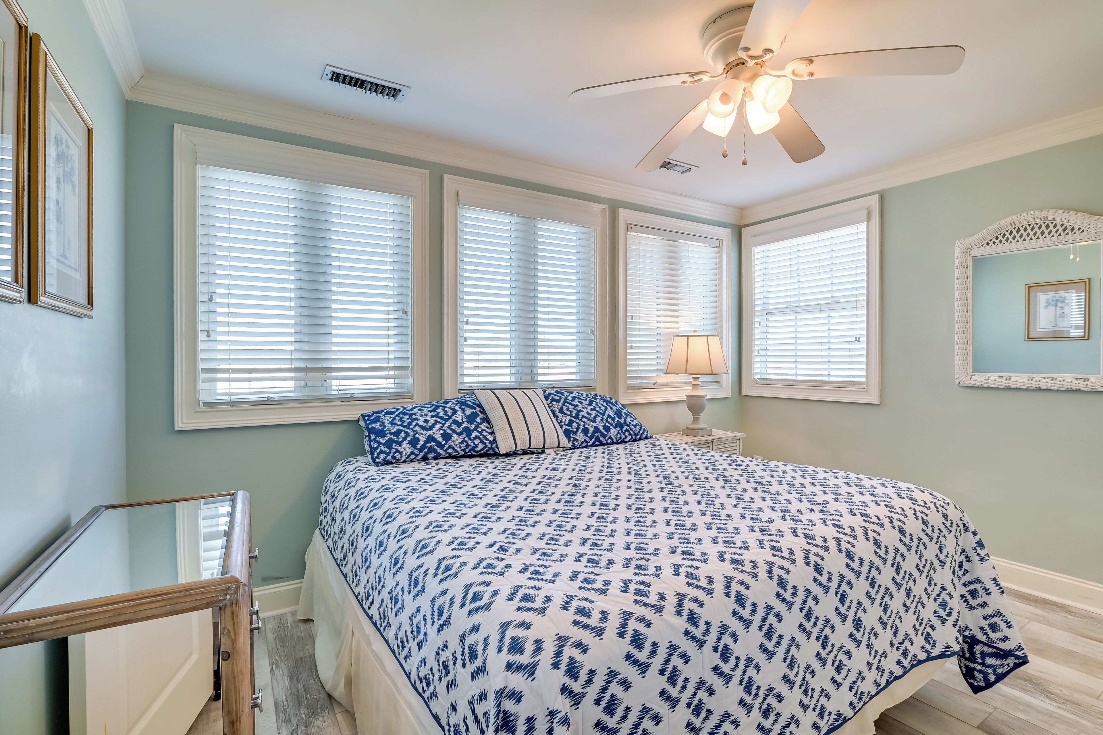 Quarto com uma cama, um ventilador de teto e três janelas com cortinas.