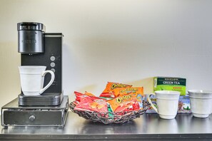Uma cafeteira, um cesto de lanches e uma caixa de chá verde sobre uma mesa.