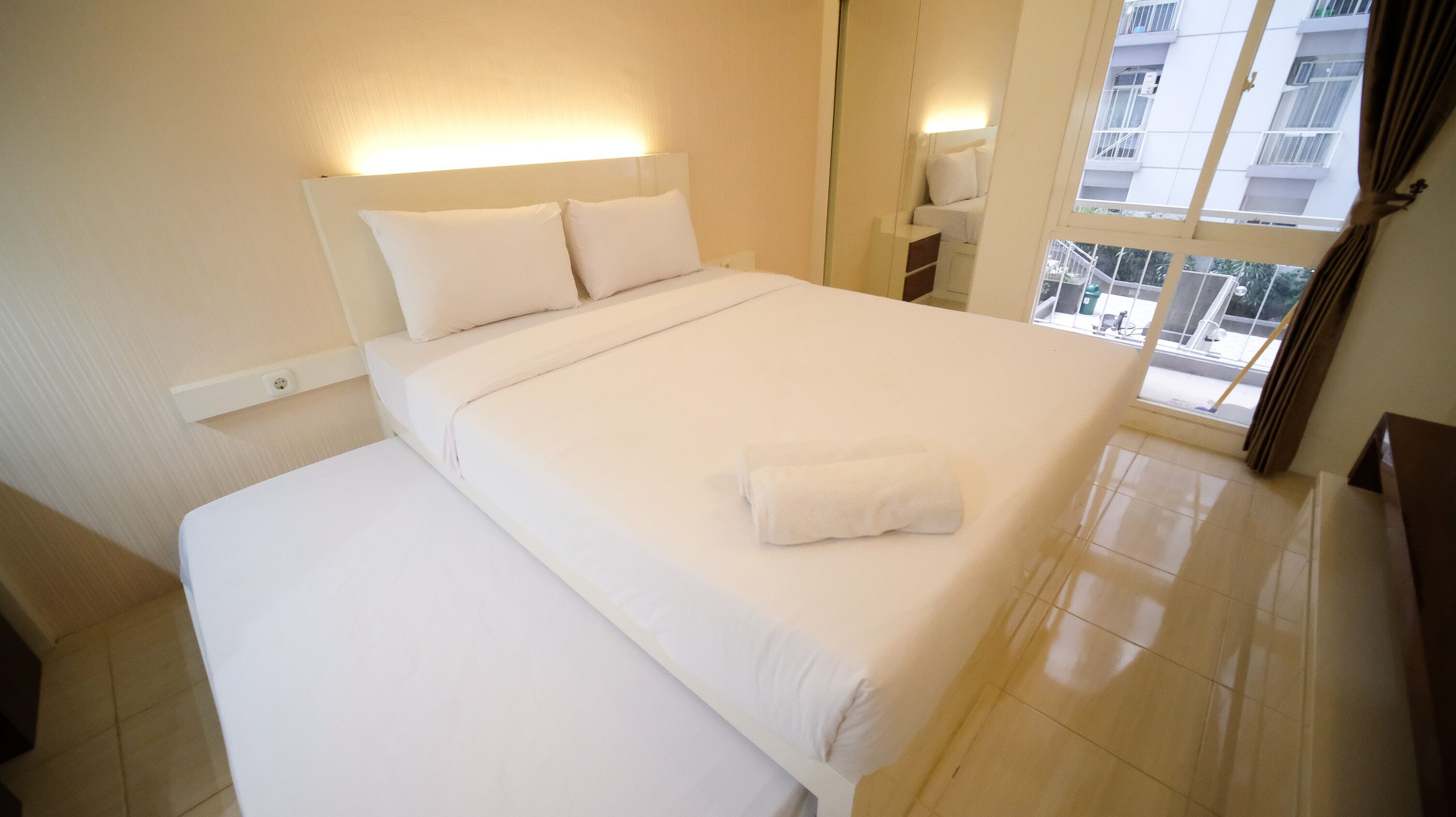 Quarto de hotel com uma cama grande, uma mesa de cabeceira, uma janela com vista para edifícios e uma cortina.