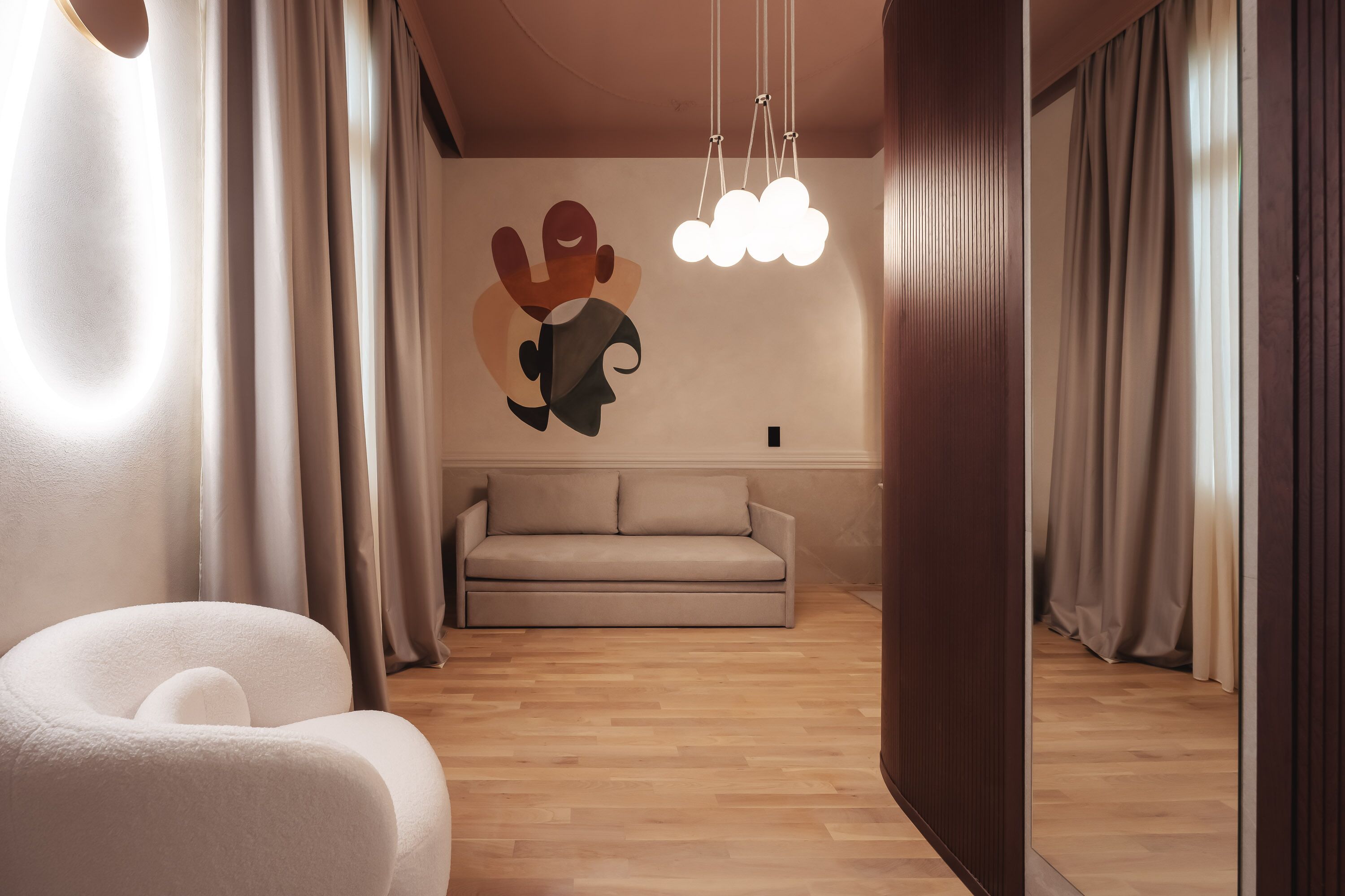 Uma sala de estar moderna com um sofá, uma poltrona branca e um lustre fixado na parede.
