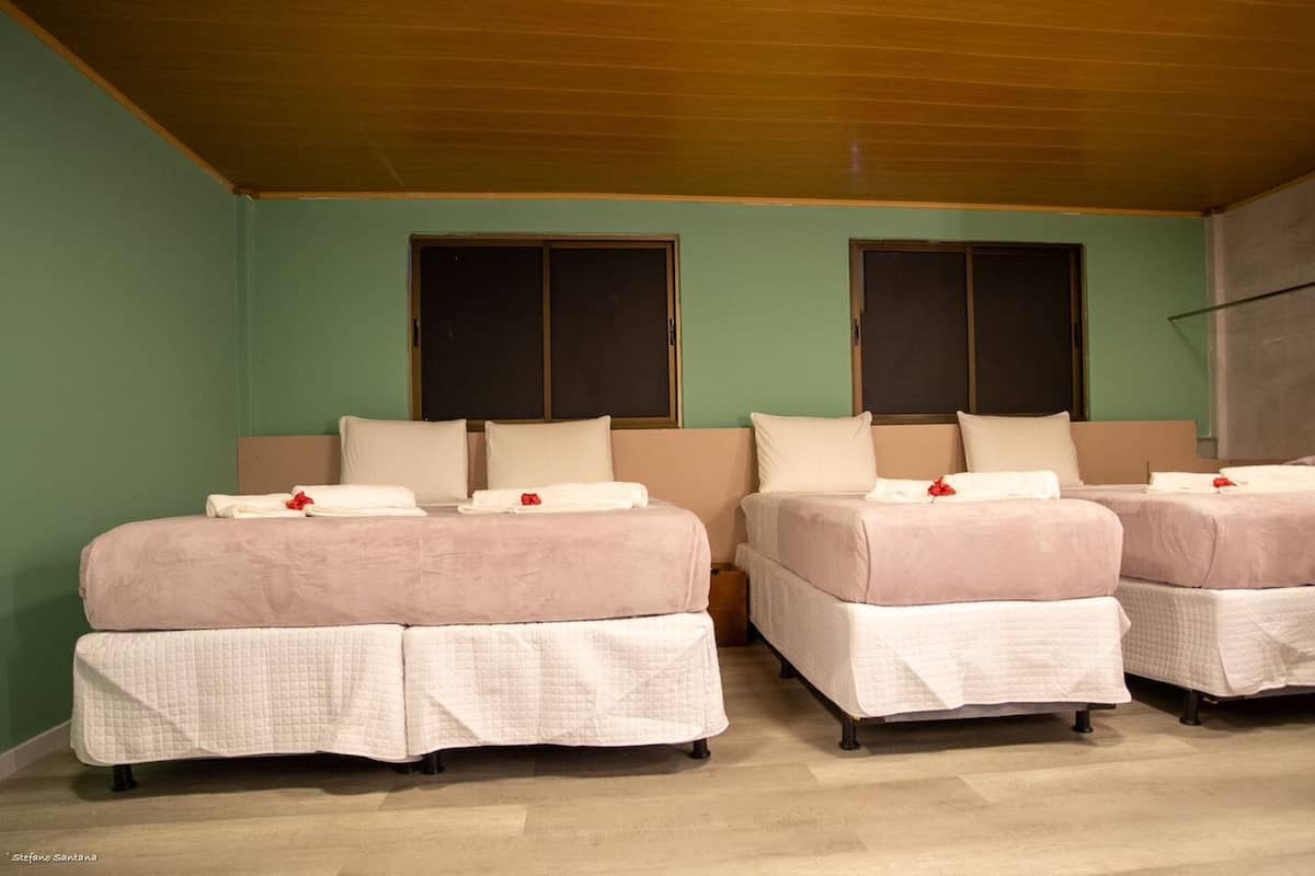 Quarto com duas camas, cada uma com colcha acolchoada branca e almofadas, e teto de madeira.