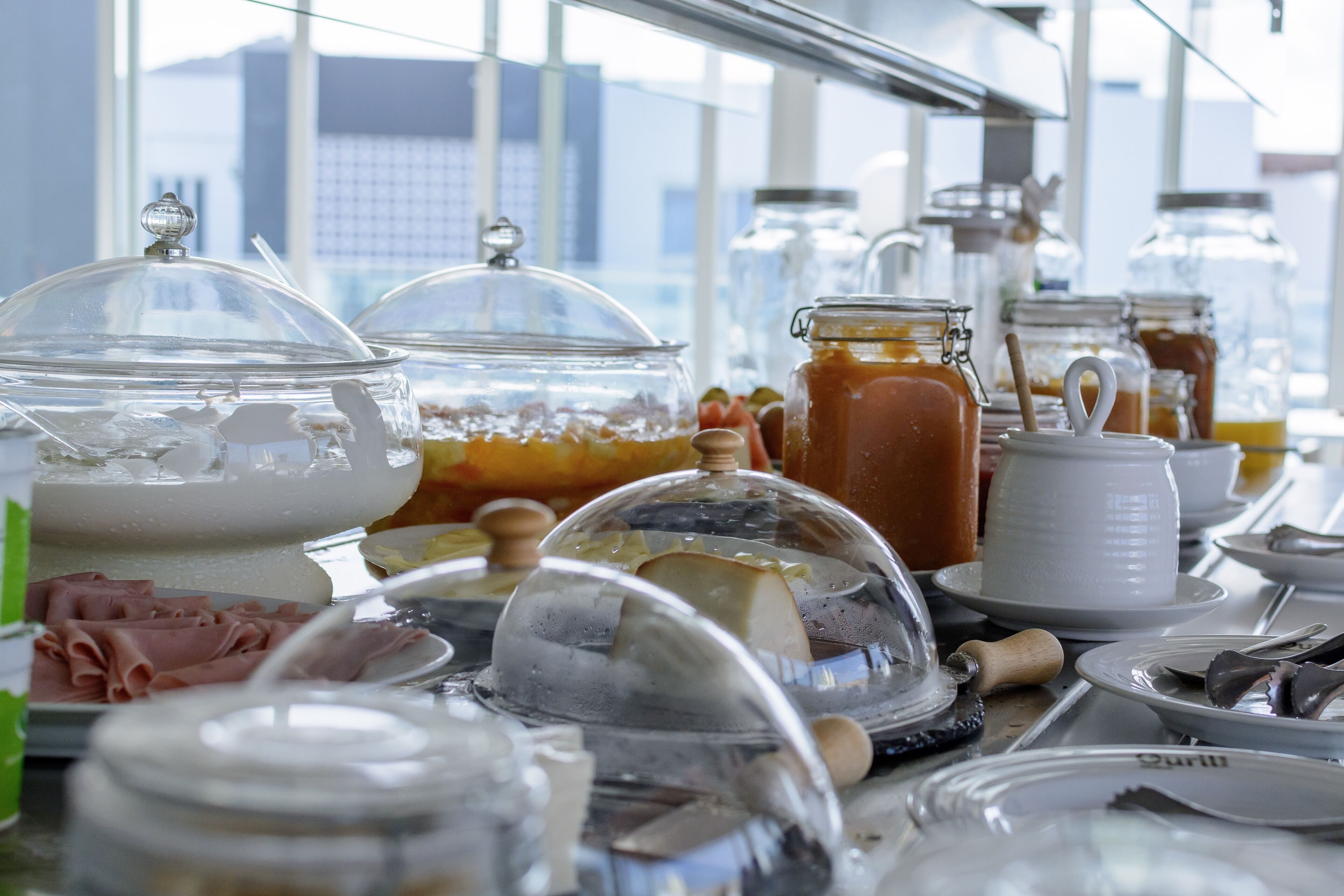 Disposição de buffet com diversos alimentos e acompanhamentos, incluindo potes de molhos e uma travessa coberta.