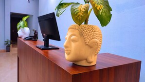 Bancada de recepção com monitor de computador, escultura de cabeça de Buda e planta em vaso.