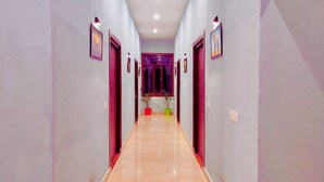 Um corredor com piso lustroso, portas vermelhas e quadros nas paredes.