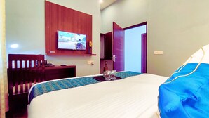 Quarto de hotel com cama, escrivaninha, televisão presa à parede e porta que dá para outro cômodo.