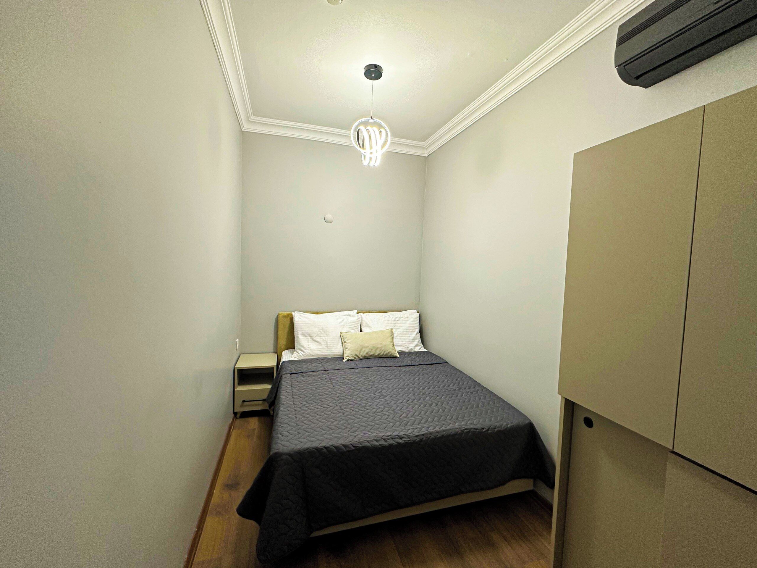 Quarto com cama, mesas de cabeceira, guarda-roupa e luminária no teto.