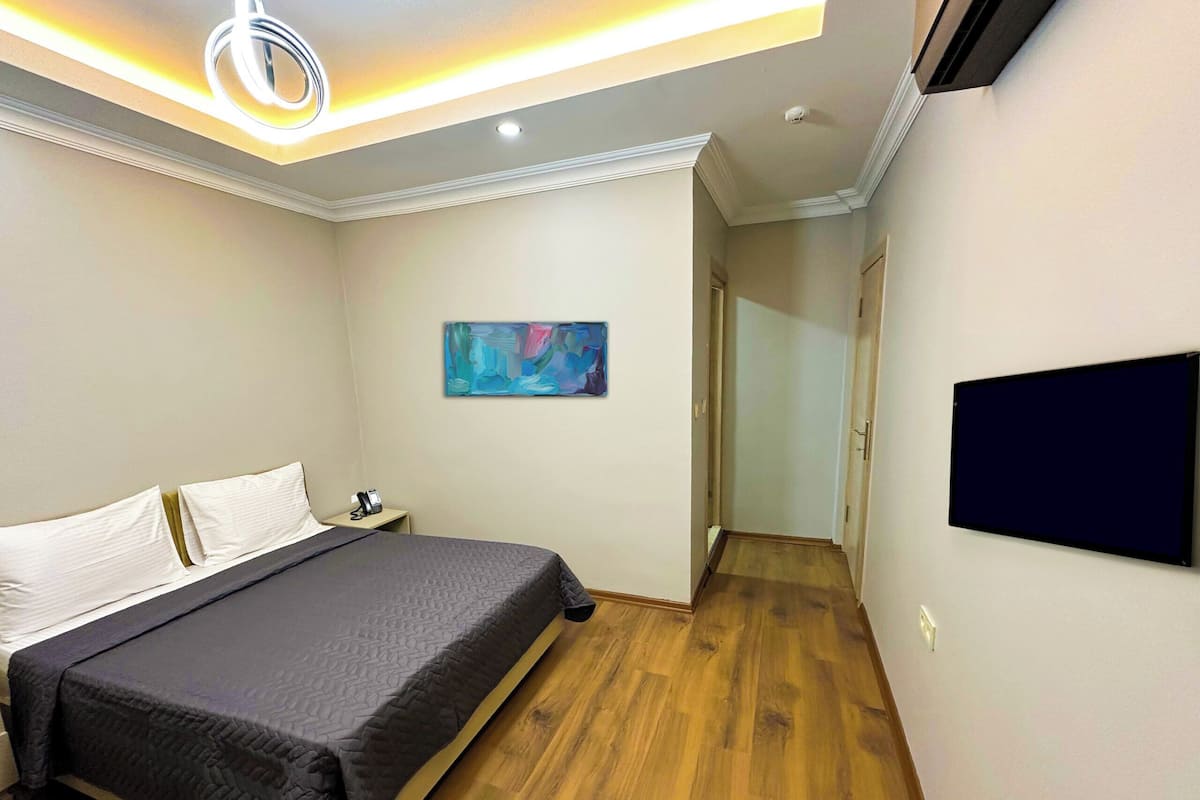 Quarto de hotel com uma cama, um quadro, um telefone na mesa de cabeceira e uma televisão na parede.