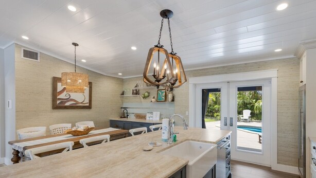 Uma cozinha moderna com uma ilha grande, luminária pendente e vista para uma piscina através de uma porta aberta.