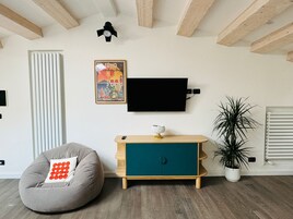 Uma sala de estar moderna com teto de madeira, um armário verde-água, um bean bag cinza, uma planta em vaso e uma TV fixada na parede.