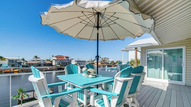 Um terraço com mesa, cadeiras, guarda-sol e vista para o mar e edifícios.