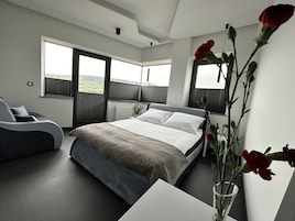 Quarto moderno com uma cama grande, um sofá e vista para o exterior pelas janelas.