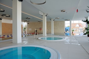 Piscina interna com várias pistas de natação, um posto de salva-vidas e uma ampla vista do exterior através de grandes janelas.