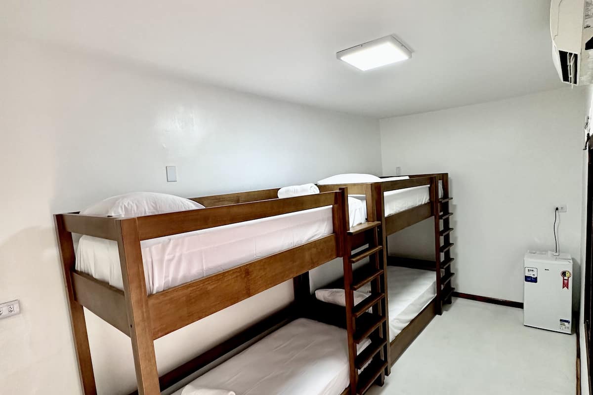 Quarto com beliche, paredes brancas, iluminação no teto e aquecedor.