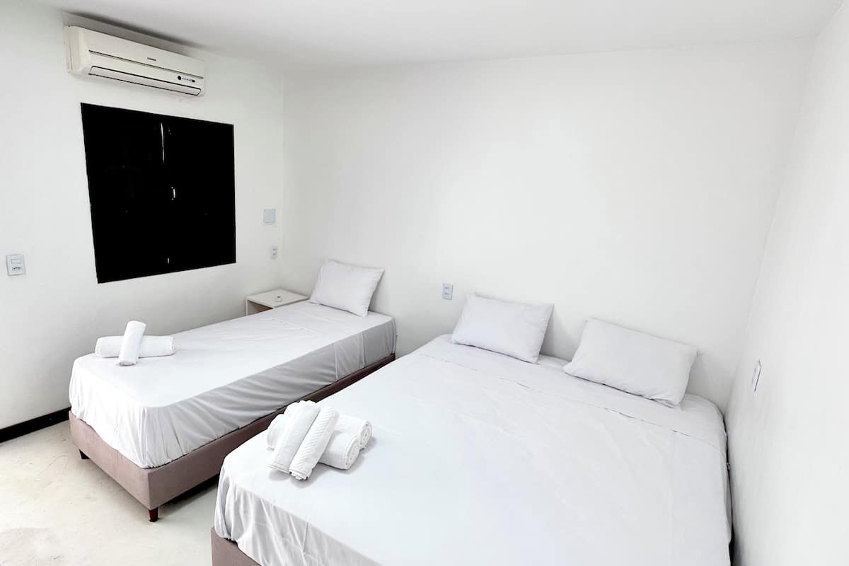 Quarto de hotel com duas camas, roupa de cama branca, TV de tela plana na parede e aparelho de ar condicionado.