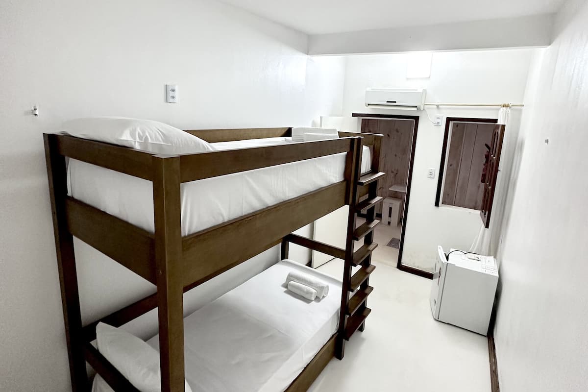 Quarto com beliche, parede branca, pequeno armário branco e aquecedor branco.