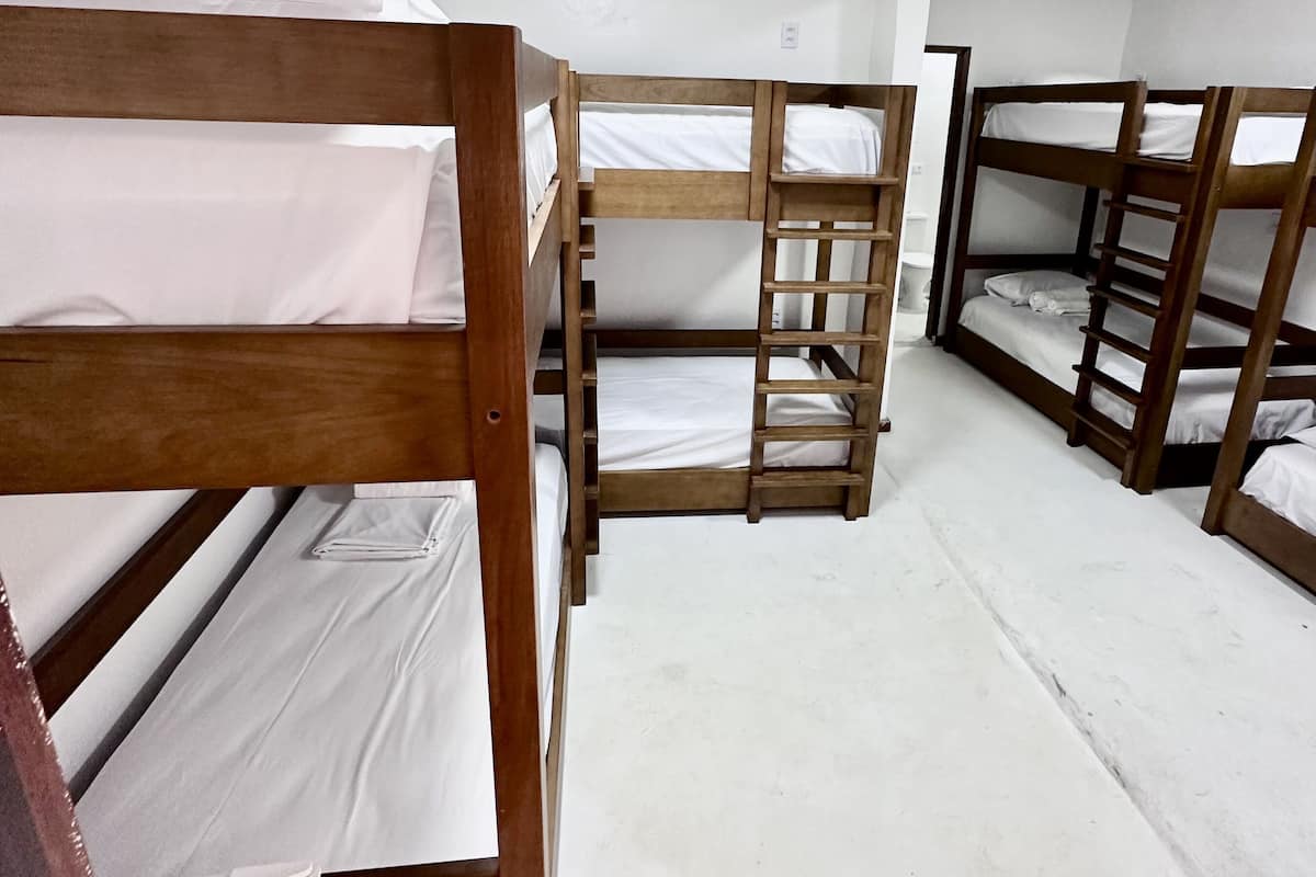 Quarto em dormitório com beliches, claraboia e piso branco.