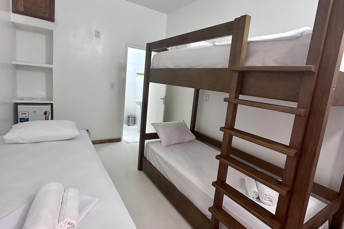 Quarto com beliches, pia e prateleira com produtos de higiene pessoal.