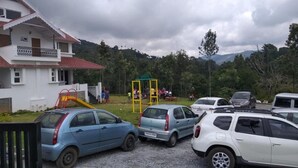 Uma área de estacionamento com vários carros, um parquinho e um edifício com telhado vermelho.