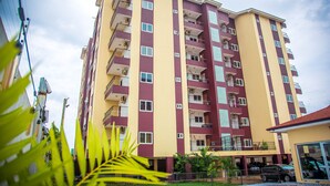 Um edifício com vários andares, varandas, área de estacionamento e um pequeno jardim.