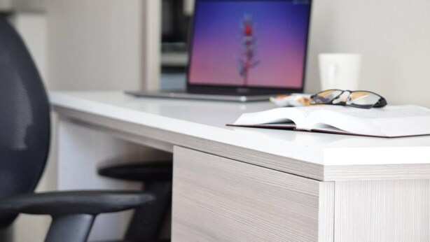 Uma mesa de escritório moderna com um laptop, um livro aberto e um par de óculos.