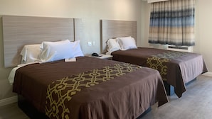 Quarto de hotel com duas camas, cada uma com colcha estampada, uma mesa de cabeceira com telefone e uma janela com cortina.