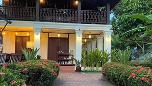 Um edifício de dois andares com varanda, caminho de tijolos e plantas em vasos.