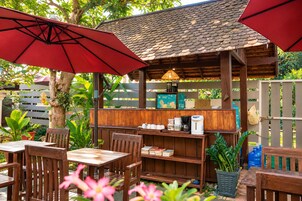 Café ao ar livre com móveis de madeira, guarda-sóis vermelhos e um espaço para café.