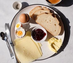 Prato de café da manhã com pão, ovos, queijo, manteiga e geleia.
