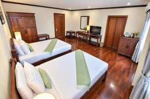 Quarto de hotel com duas camas, uma escrivaninha e televisão, e armários de madeira.