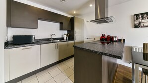 Uma cozinha moderna com ilha central, eletrodomésticos de aço inoxidável e bancada preta.