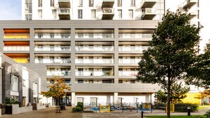 Um edifício residencial com vários andares, varandas, um parquinho fechado e uma árvore em primeiro plano.