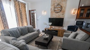 Uma sala de estar moderna com um sofá cinzento, uma mesa de centro e uma televisão de tela plana presa a uma parede de tijolos.