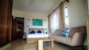 Quarto com cama, mesa de cabeceira de madeira, sofá e uma janela grande com cortinas.
