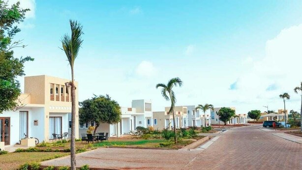Uma fileira de edifícios modernos, térreos e com telhados planos, dispostos ao longo de uma rua pavimentada.