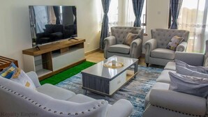 Uma sala de estar com uma TV de tela plana, duas poltronas, um sofá e uma mesa de centro.