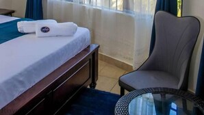 Quarto de hotel com uma cama, uma cadeira, uma mesinha e uma janela com cortinas.