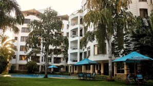 Um hotel com vários andares, piscina, área de estar externa e palmeiras.