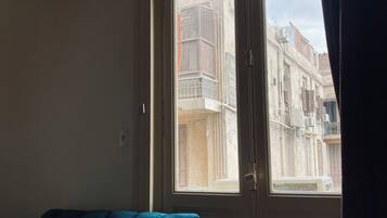 Quarto com um sofá azul, uma janela com vista para edifícios e um aparelho de ar condicionado.