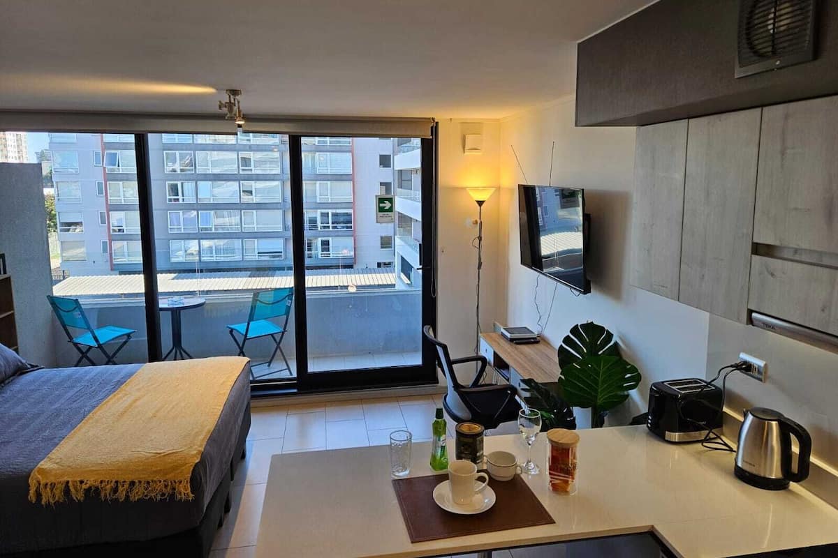 Quarto de hotel moderno com cama, mesa de refeições com itens de café da manhã, televisão e varanda com vista para a cidade.