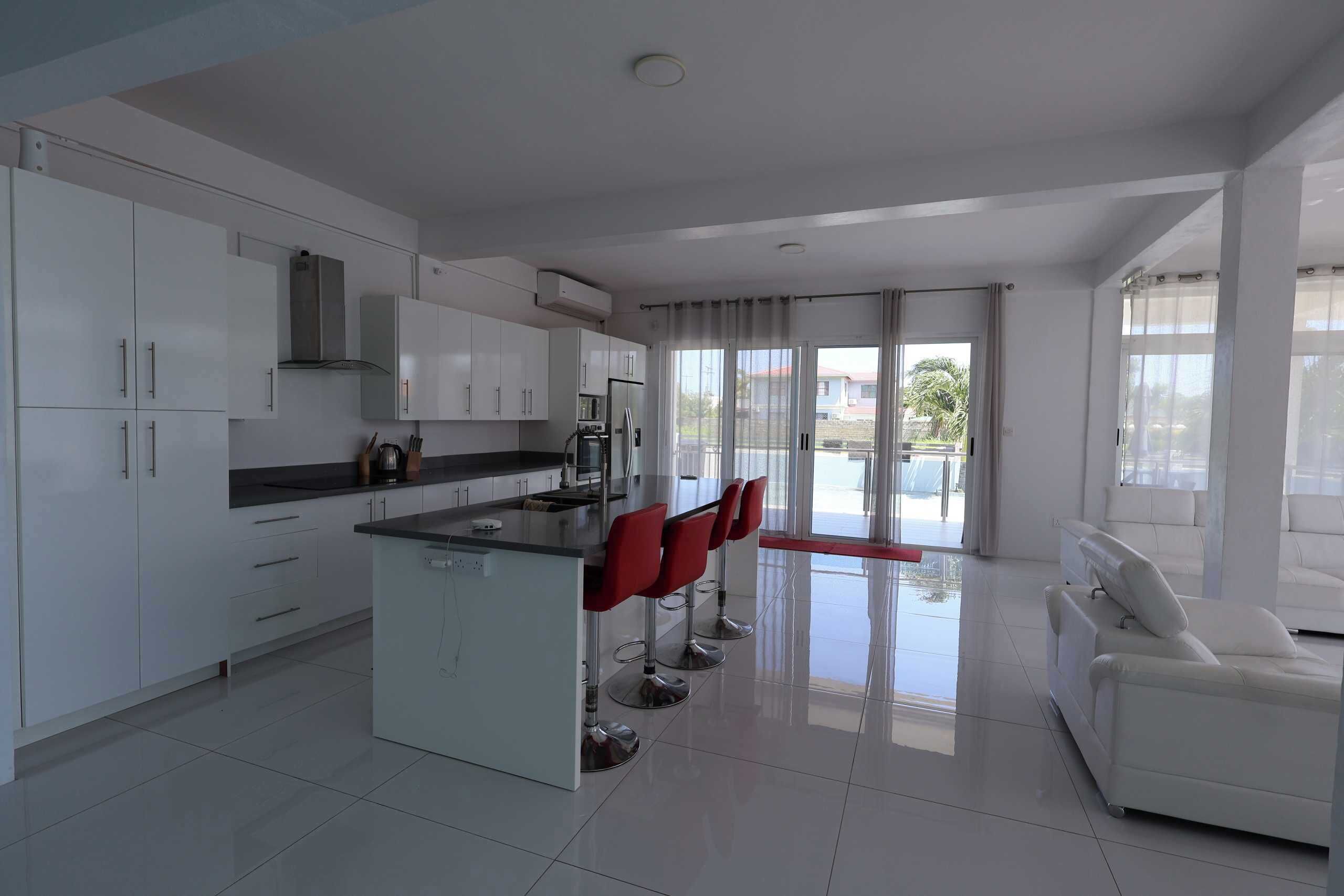 Uma cozinha moderna com armários brancos, uma ilha central com banquetas e uma janela grande com vista para o exterior.