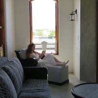 Uma mulher lendo um livro em um quarto com vista para a água e edifícios.