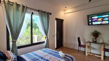 Quarto com uma cama grande, televisão fixada na parede e um espaço de refeições com mesa e cadeiras.