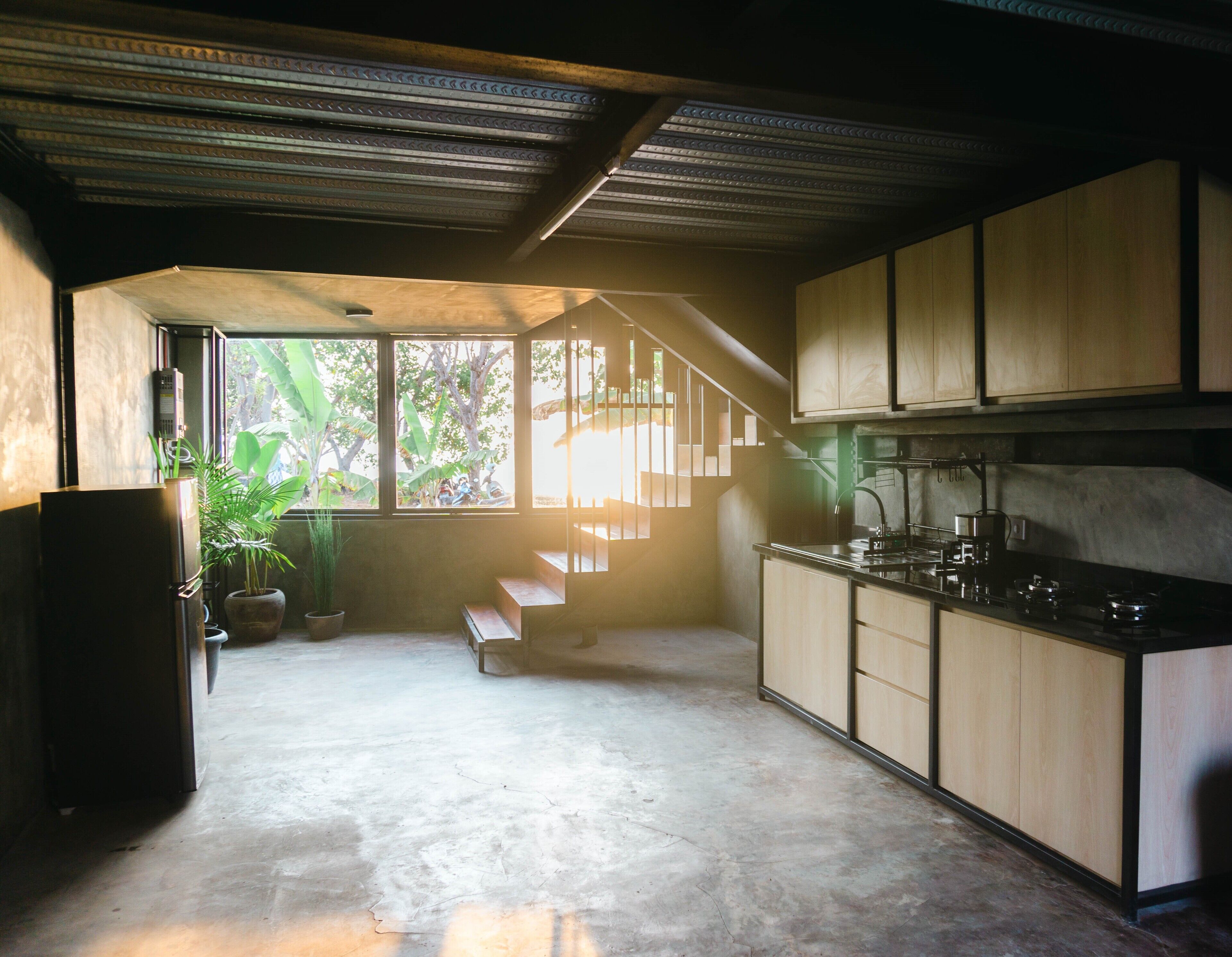 Cozinha com piso de concreto, armários de madeira e janela com vista para área verde.