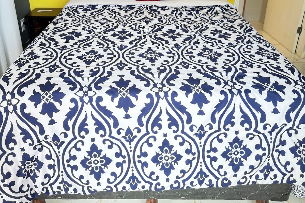 Uma cama com colcha estampada, um travesseiro vermelho e um travesseiro branco, tudo em frente a uma parede amarela.