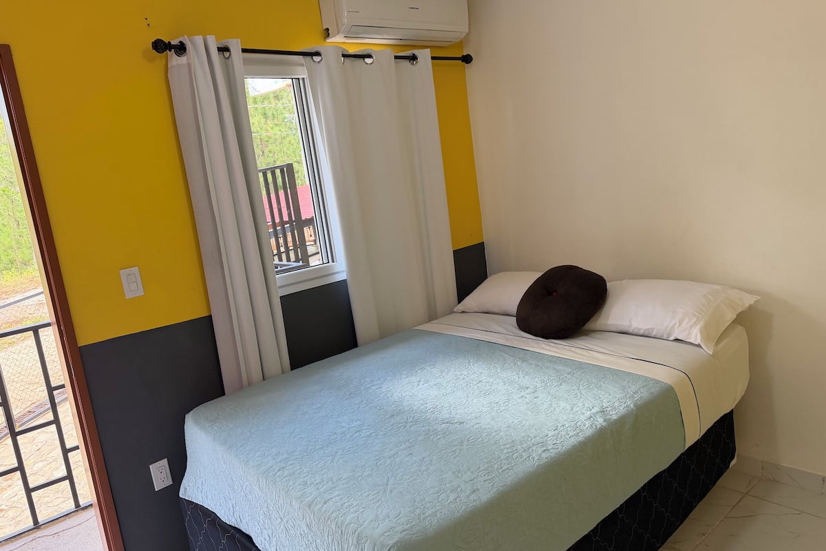 Quarto com cama, cortinas, ar condicionado e janela com vista para o exterior.