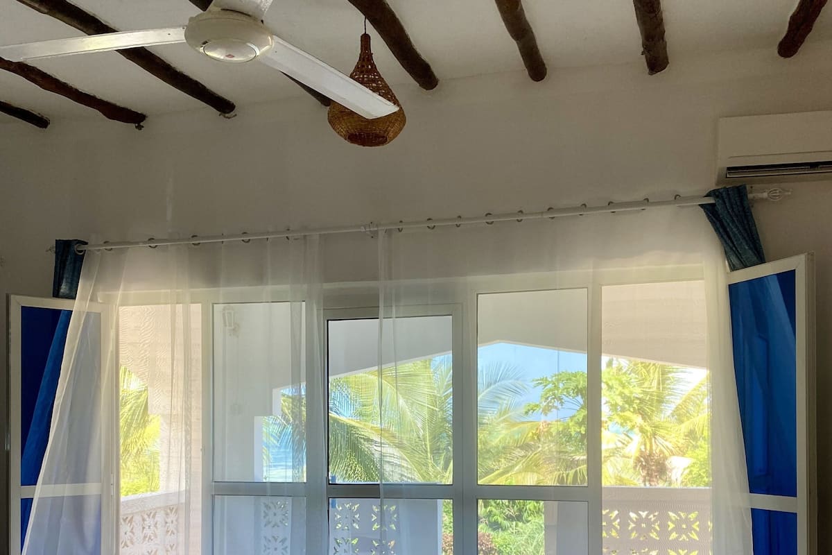 Um quarto amplo com grandes janelas, um ventilador de teto e piso revestido de azulejos.