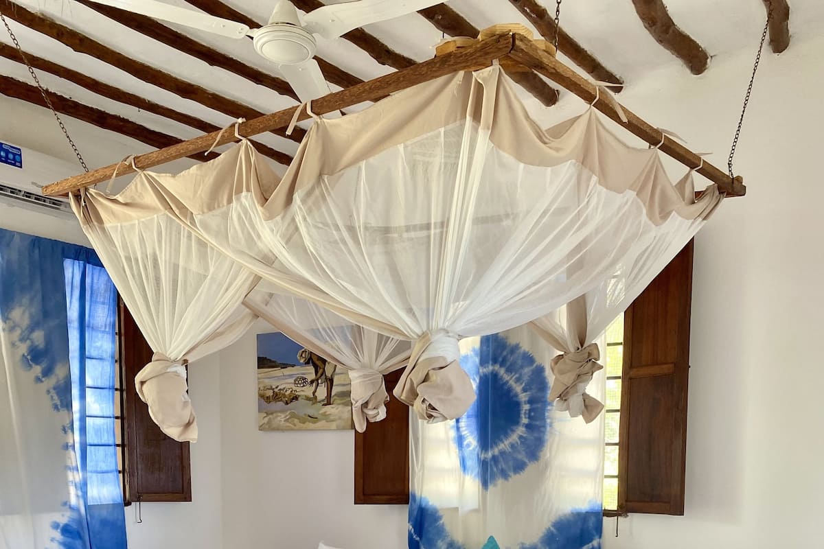 Uma cama bem arrumada com toalhas dobradas, uma cabeceira de madeira, uma mesa de cabeceira pequena de madeira e um ventilador de teto.