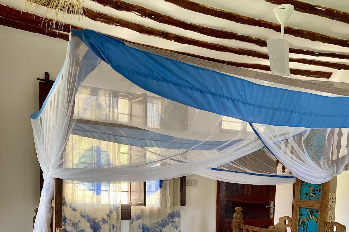 Cama com dossel, cabeceira de madeira e parede com painéis decorativos.